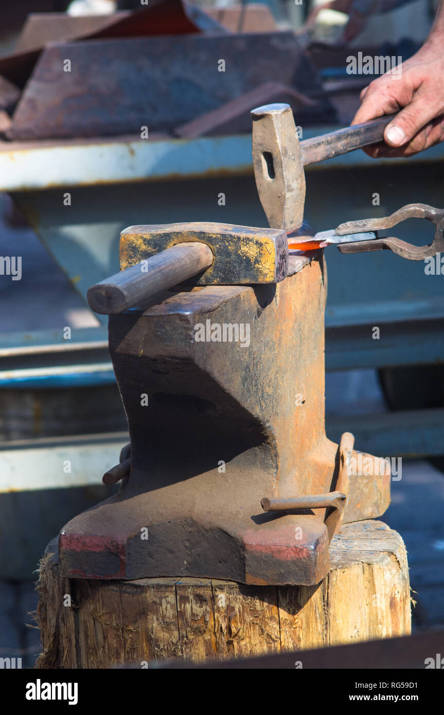 blacksmith performs the forging of hot glowing metal on the anvil ...