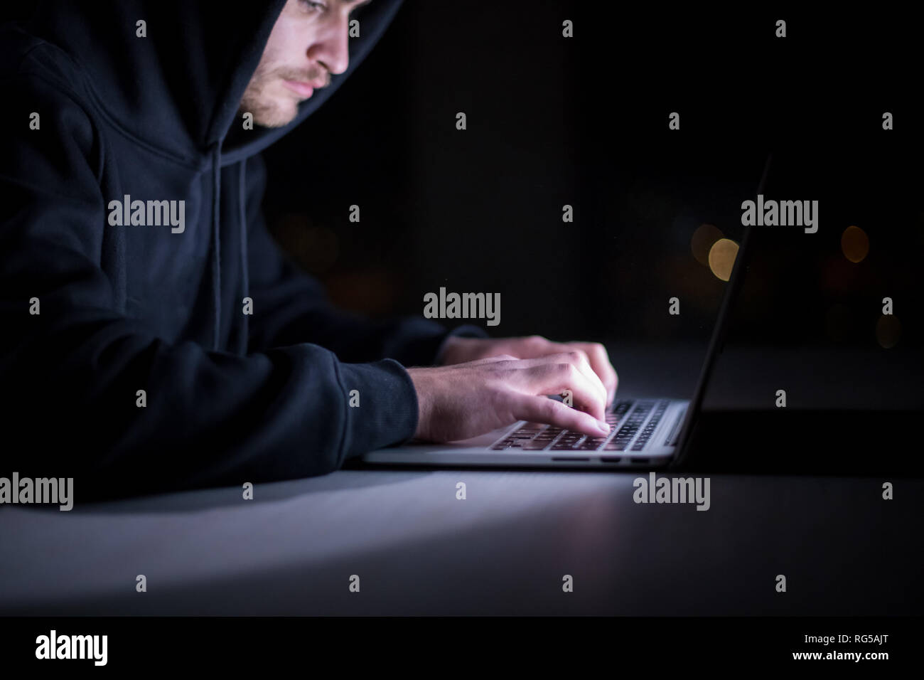 Young talented hacker using laptop computer while working in dark ...