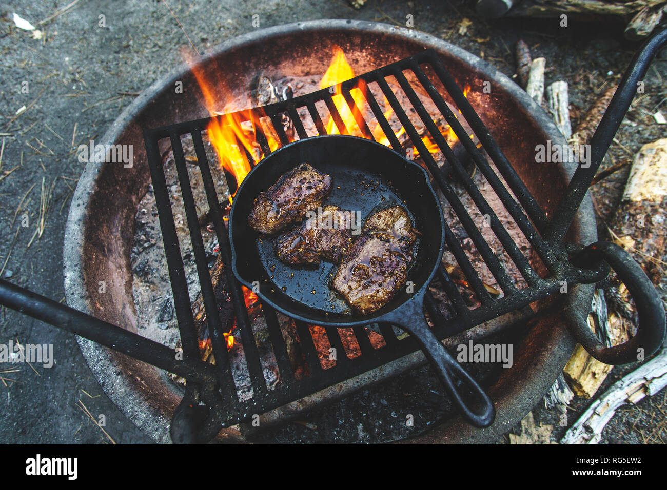 Grilling steak on cast iron over fire while camping Stock Photo - Alamy