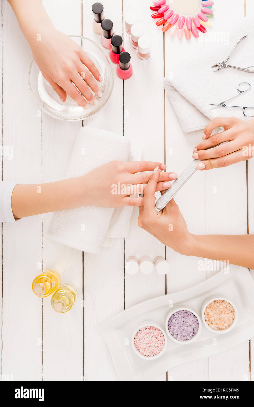 Top view of woman dipping hand in water while manicurist using nail ...