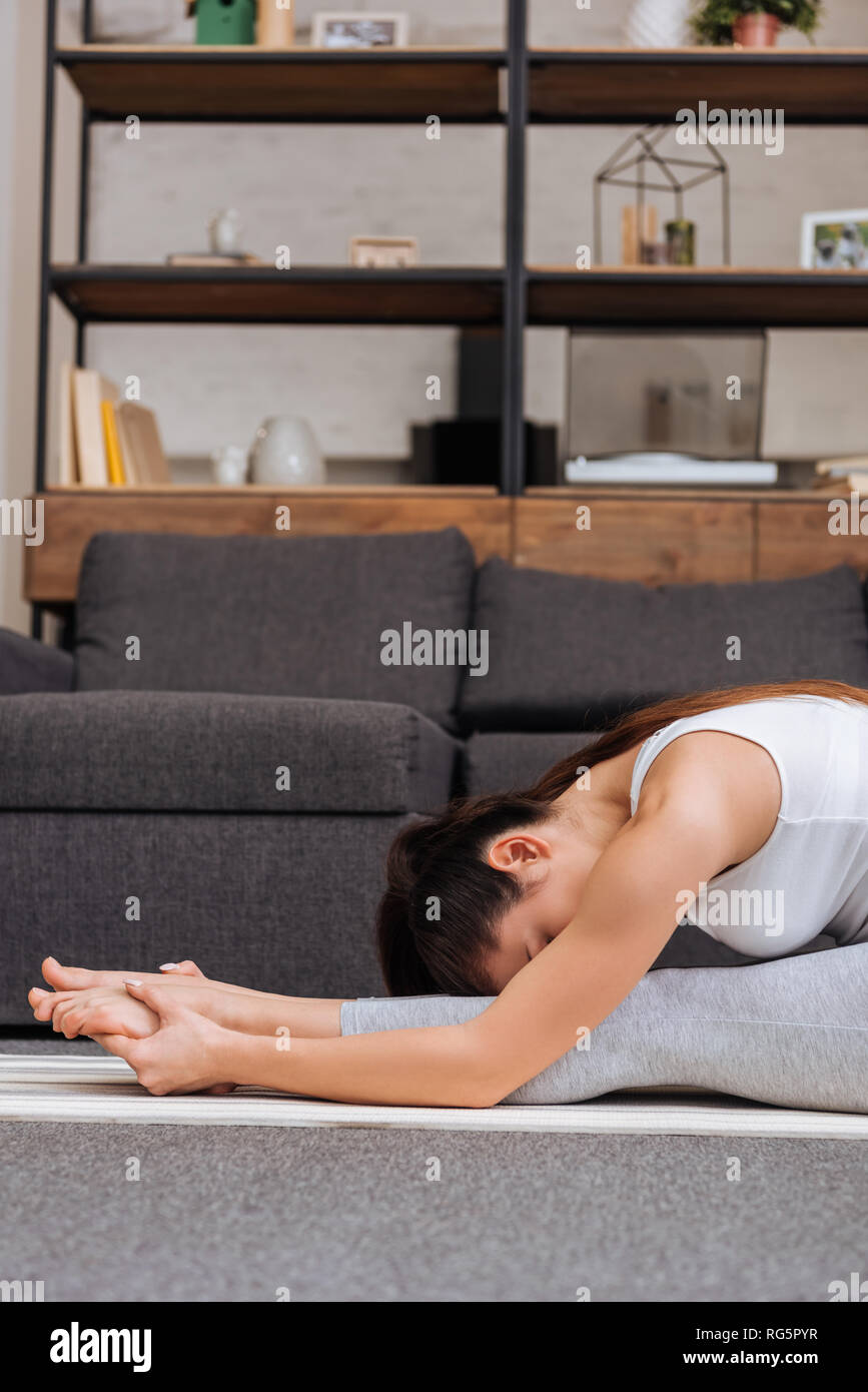 woman practicing seated forward fold pose on fitness mat at home in ...