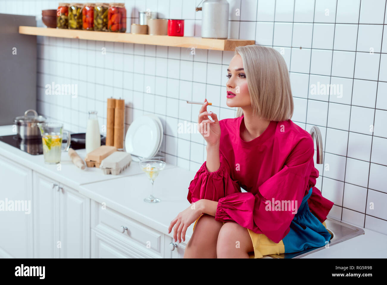 selective focus of beautiful fashionable woman sitting on kitchen ...