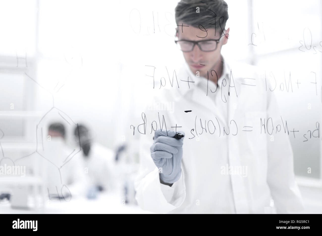serious scientist writes a chemical formula on a glass Board Stock ...