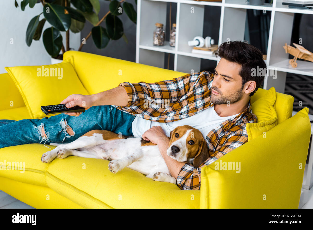 handsome man with remote control watching tv and lying on sofa with ...
