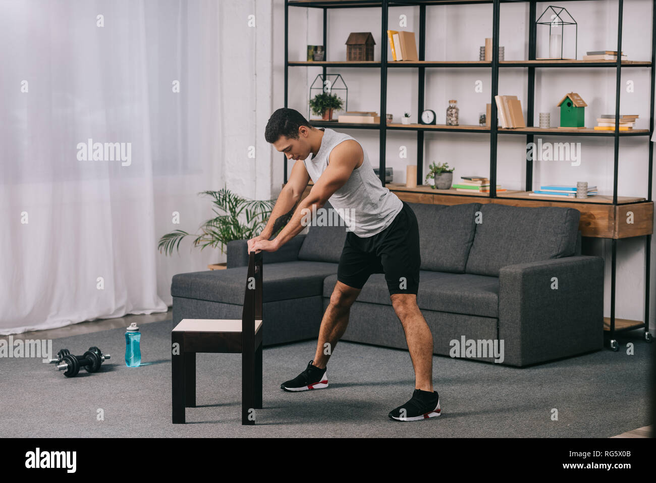 muscular mixed race athlete using chair for exercise in living room ...