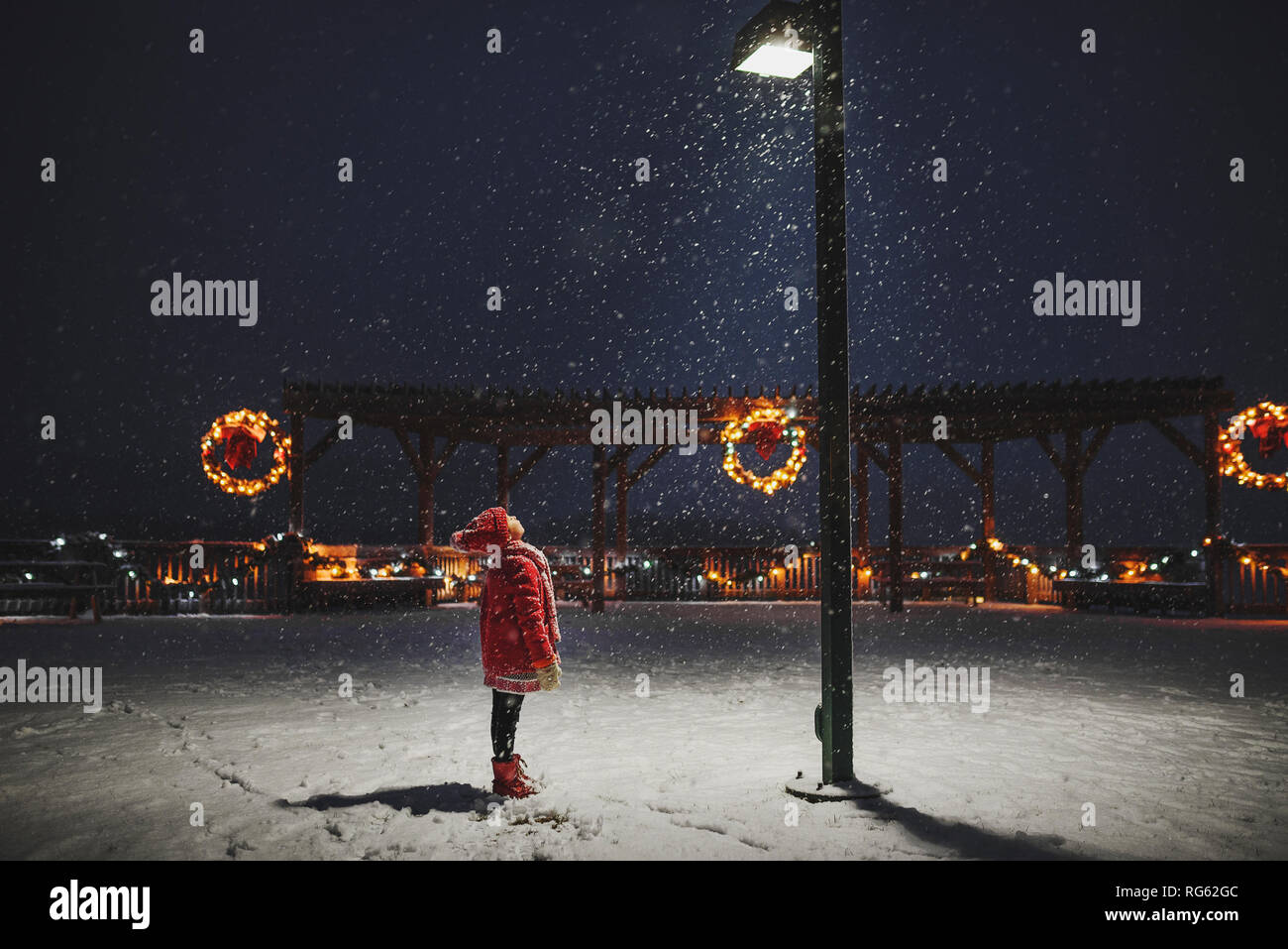 Girl standing in the snow looking up at a street lamp, United States ...