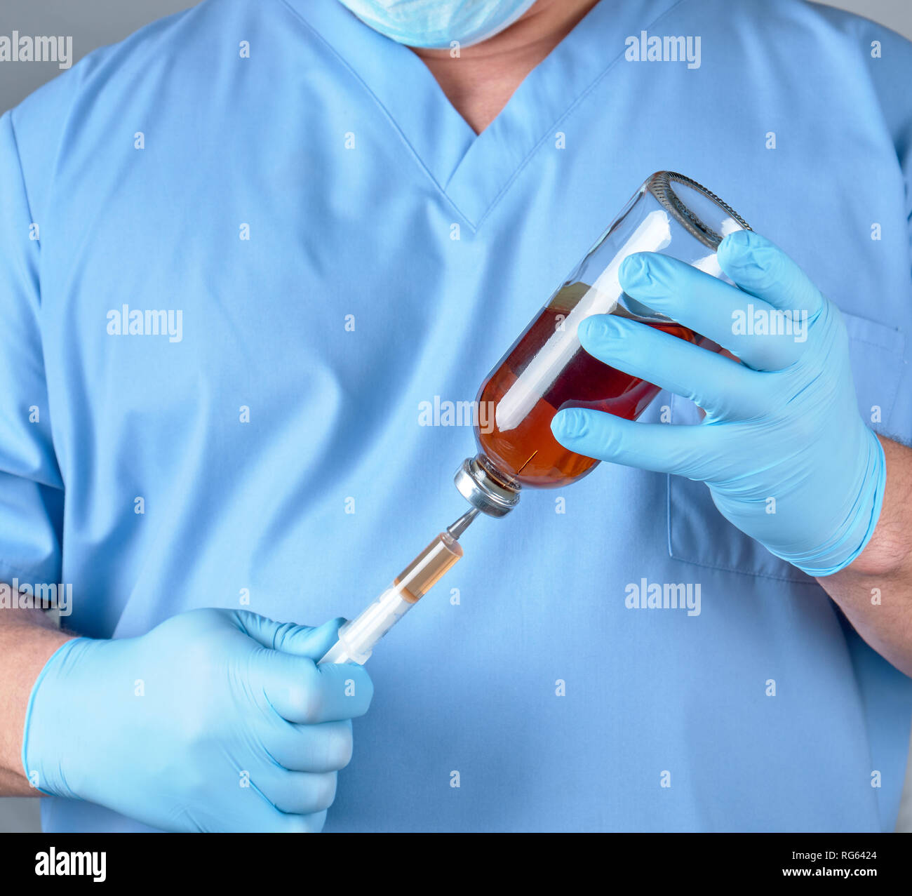 doctor in blue uniform holds a syringe and a glass bottle with ...