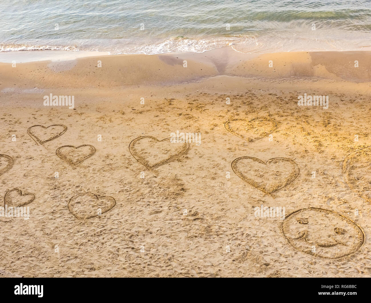 Symbols of the hearts and round face drawing on the sand on the beach ...