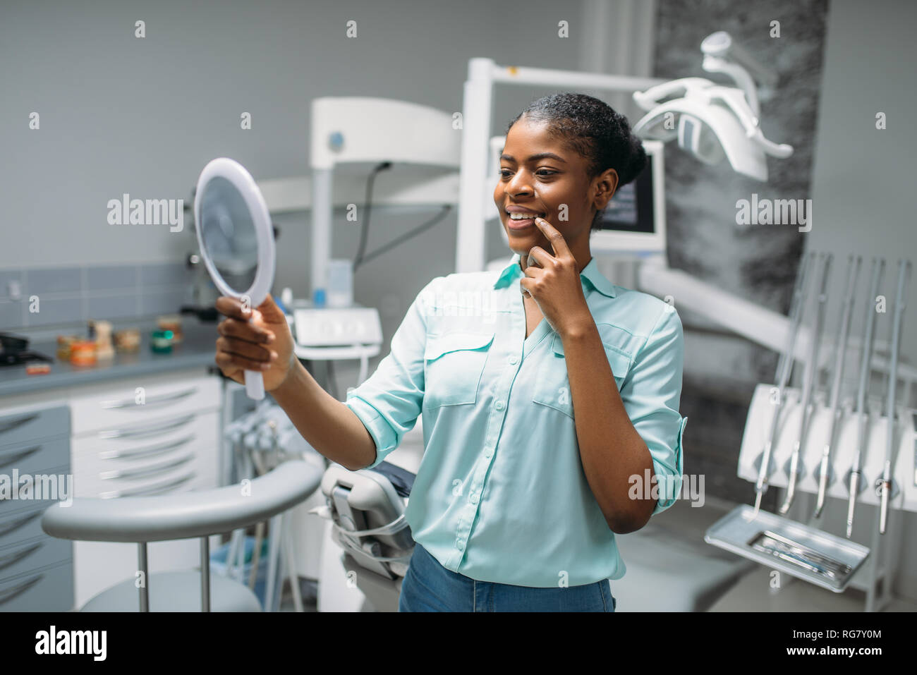 Smiling female patient looks on teeth in mirror, dental clinic, medical ...