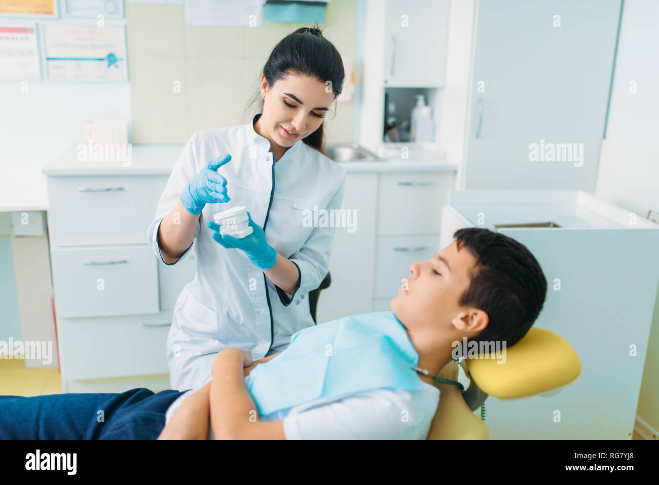 Female dentist shows dentures to little boy in a dental chair ...