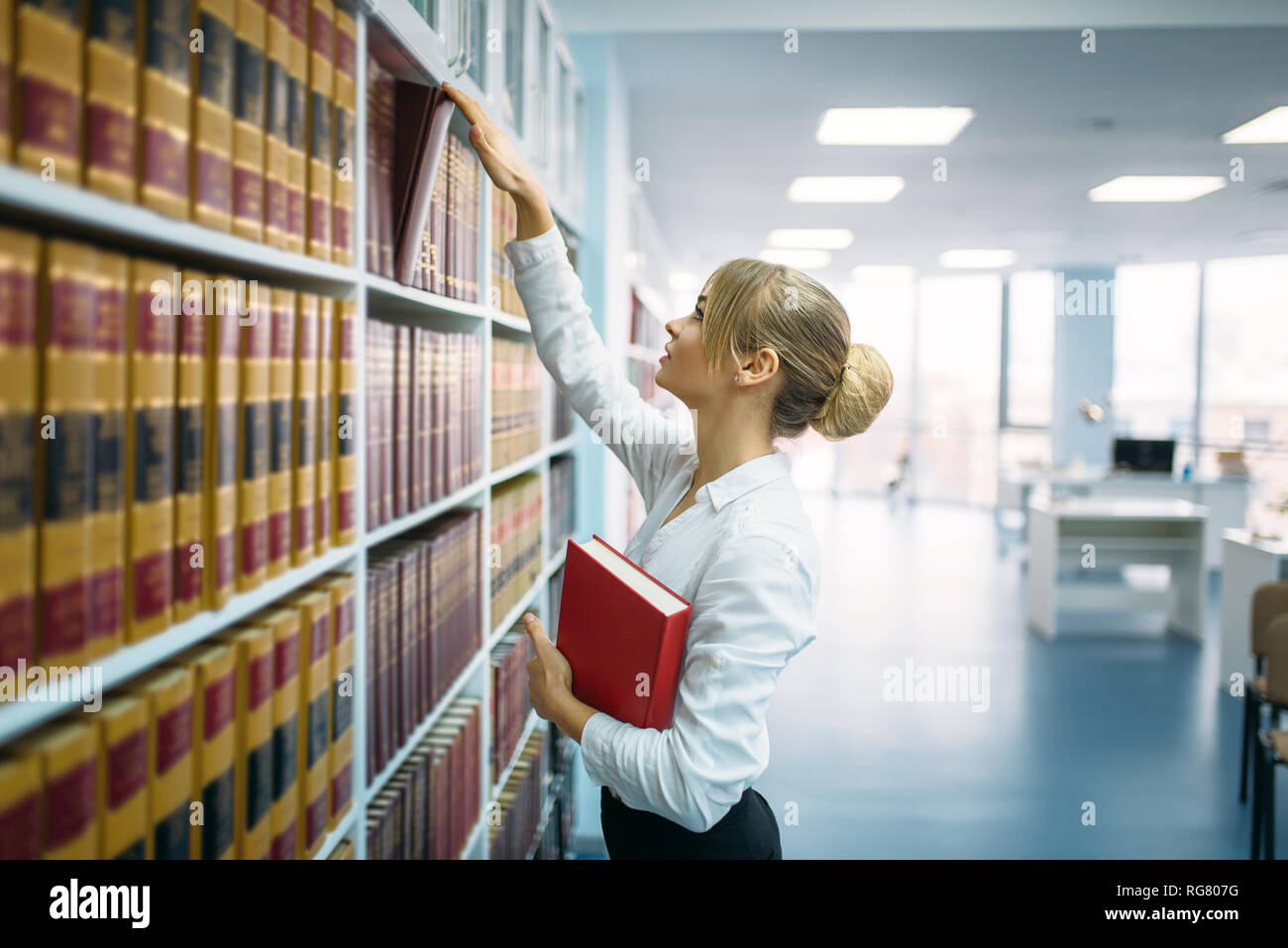 Female student looking book at the shelf in library. Young woman in ...