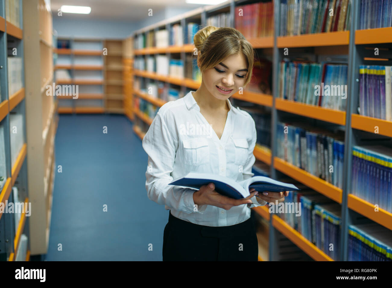 Female student with book between the shelves in university library ...