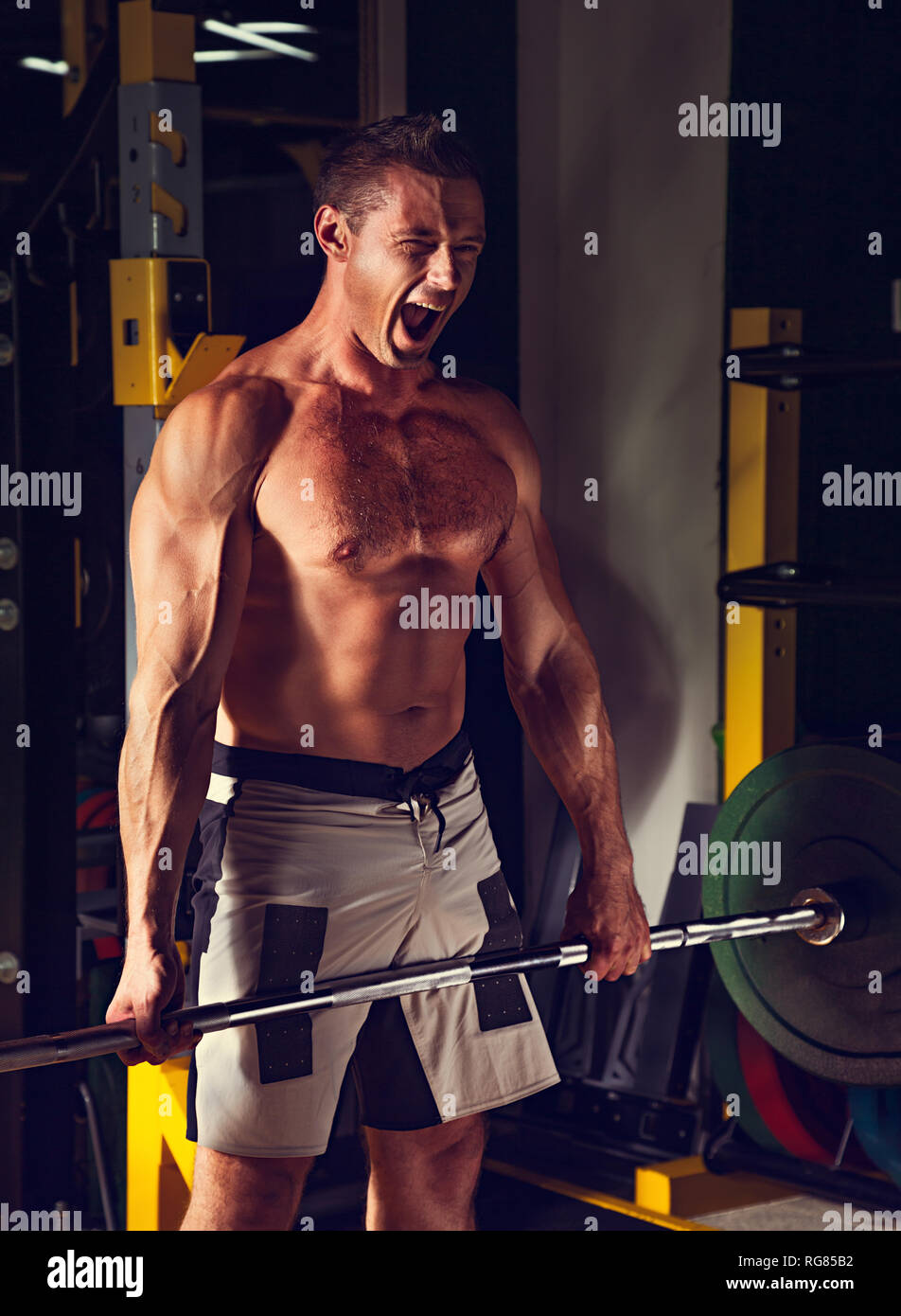 Energetic strong man lifting barbell in crossfit gym and loud agressive ...