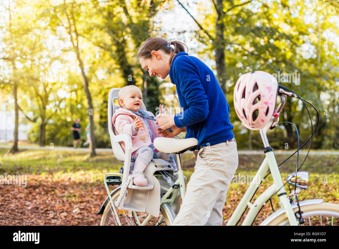 Mother and daughter riding bicycle, baby wearing helmet sitting in ...