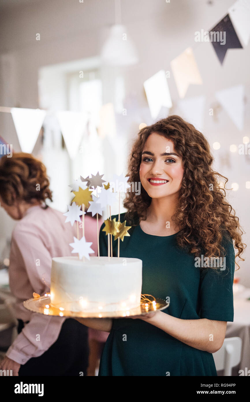 A young woman holding a birthday cake on an indoor party, family in the ...