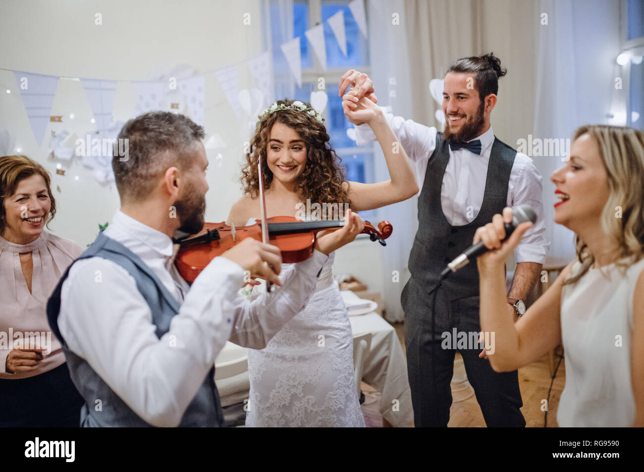 A young cheerful bride, groom and other guests dancing, singing and ...