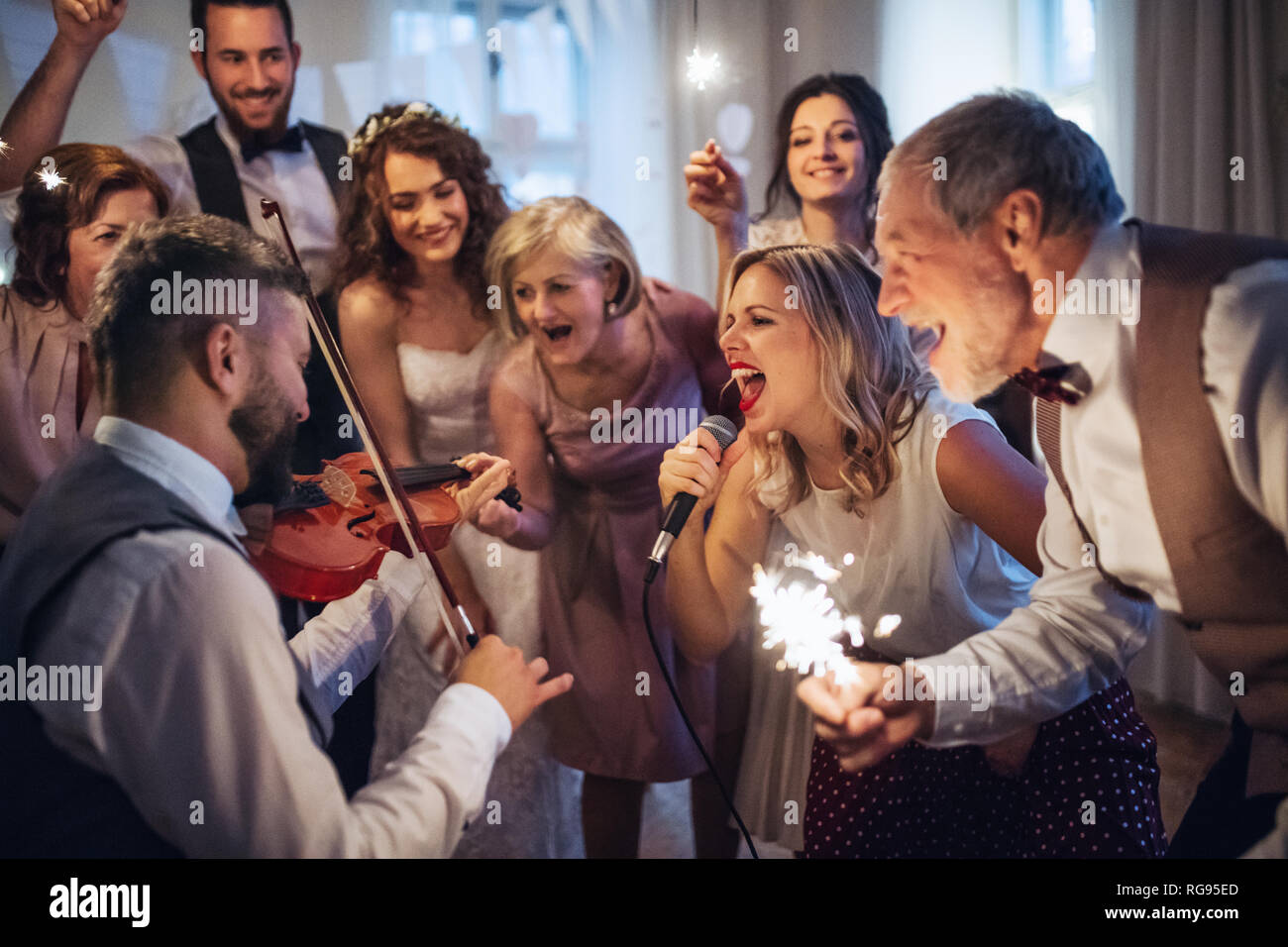 A young cheerful bride, groom and other guests dancing, singing and ...