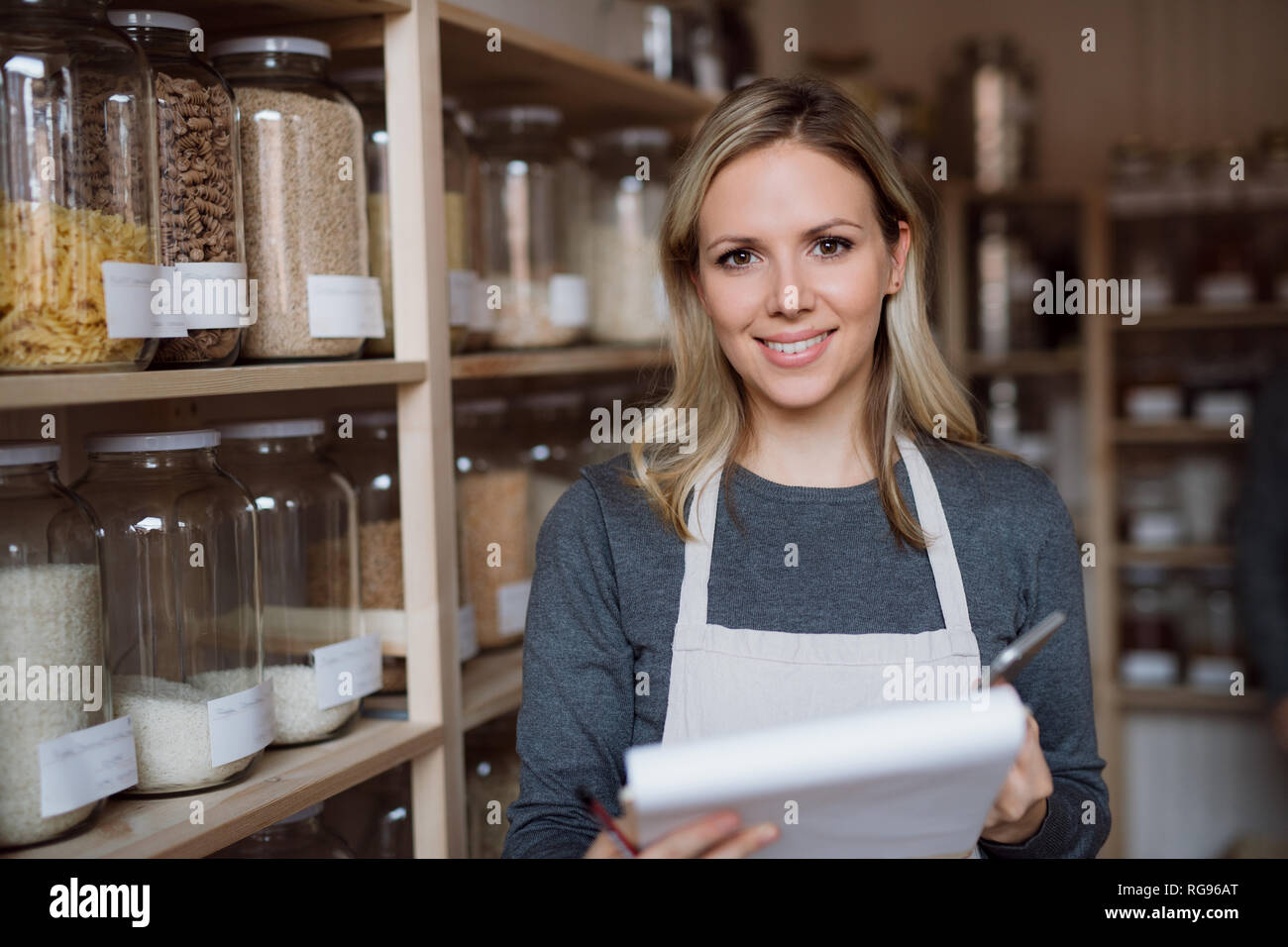 A female shop assistant with smartphone working in a zero-waste shop ...