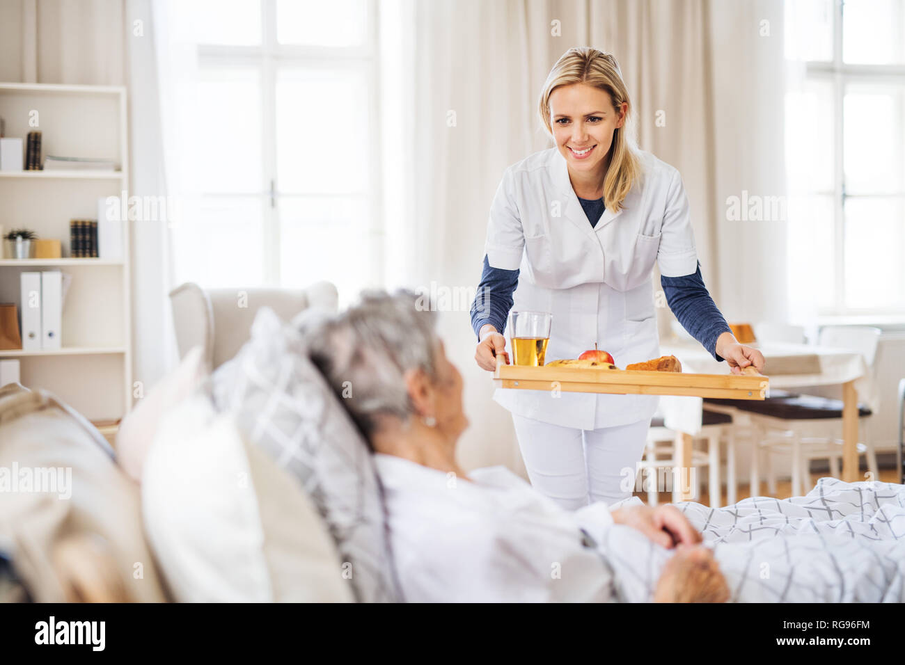A young health visitor bringing breakfast to a sick senior woman lying ...