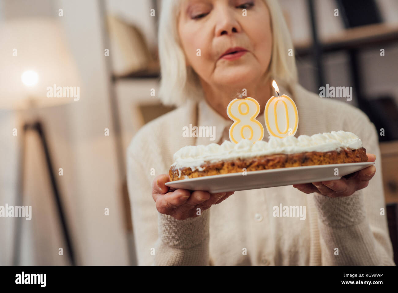 Senior Woman Blowing Out Candles On Cake With Number 80 On Top While
