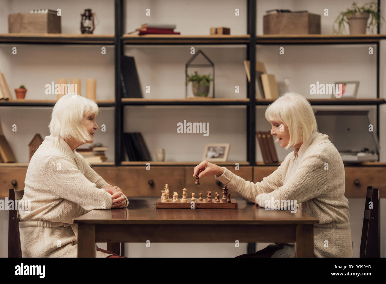 smiling senior female twins playing chess together in living room Stock ...