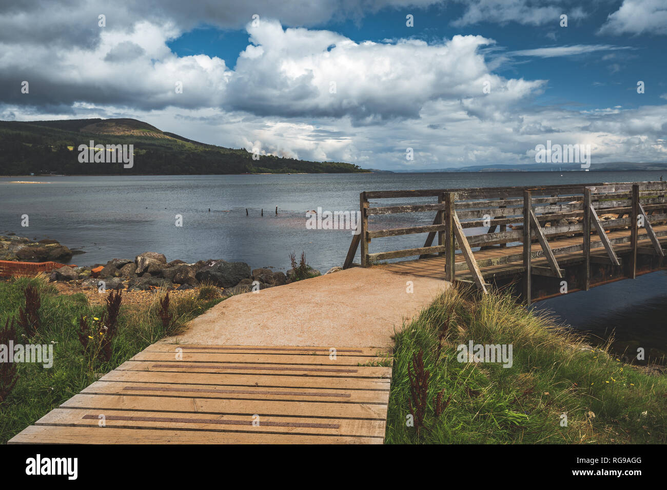 Close-up wooden pier connecting the sea and grass covered land ...
