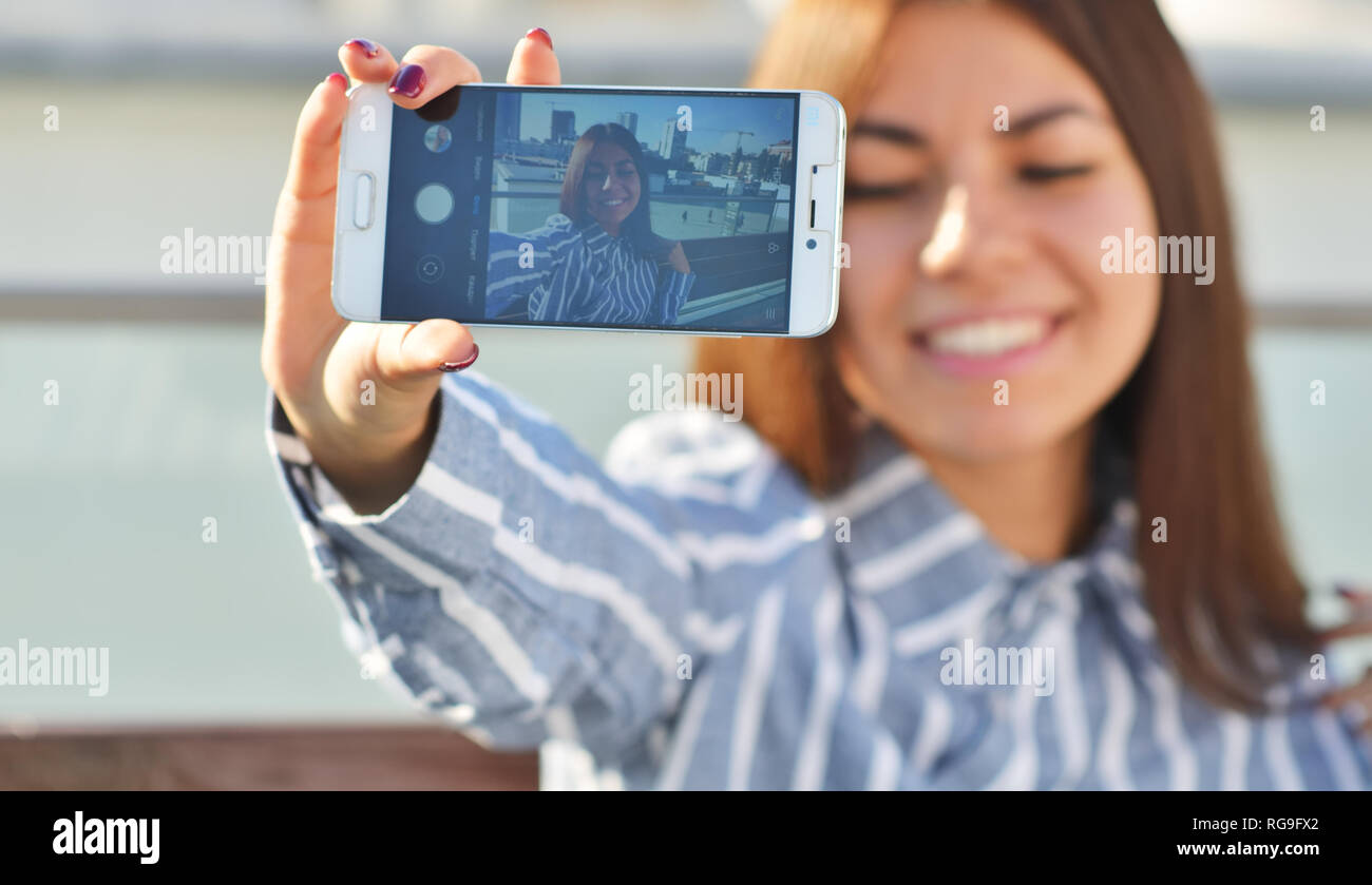 Attractive girl student smiles with her eyes closed and takes a selfie ...