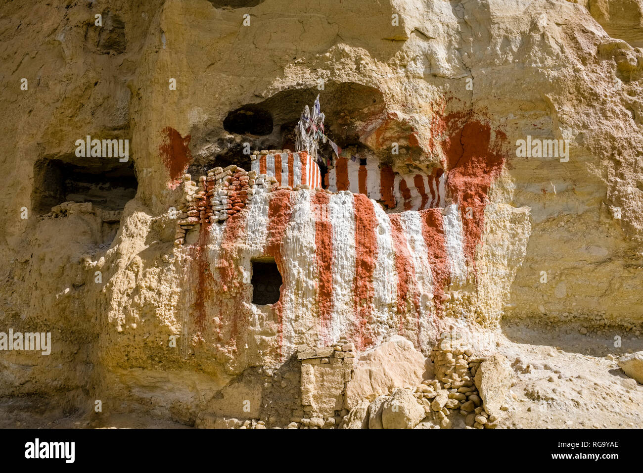 A red and white painted buddhist cave shrine, located in a rock cliff ...