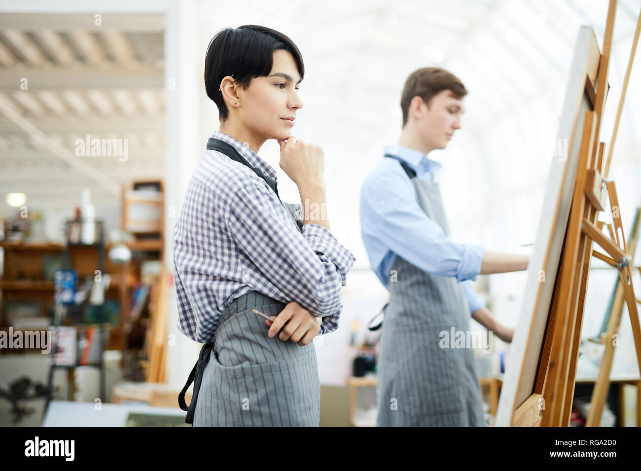 Side view portrait of young female artist standing by easel in art ...