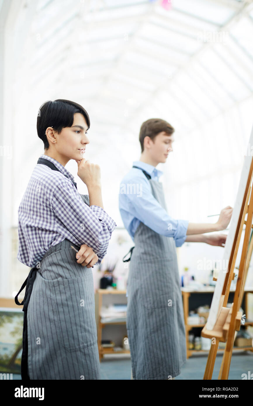 Side view portrait of young female artist standing by easel in art ...