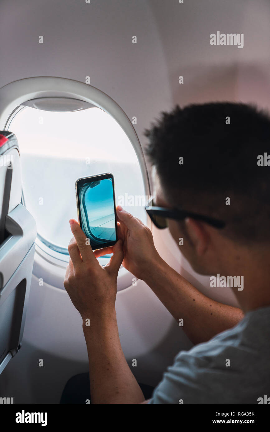 Man in airplane, using smartphone, taking a picture, airplane window ...