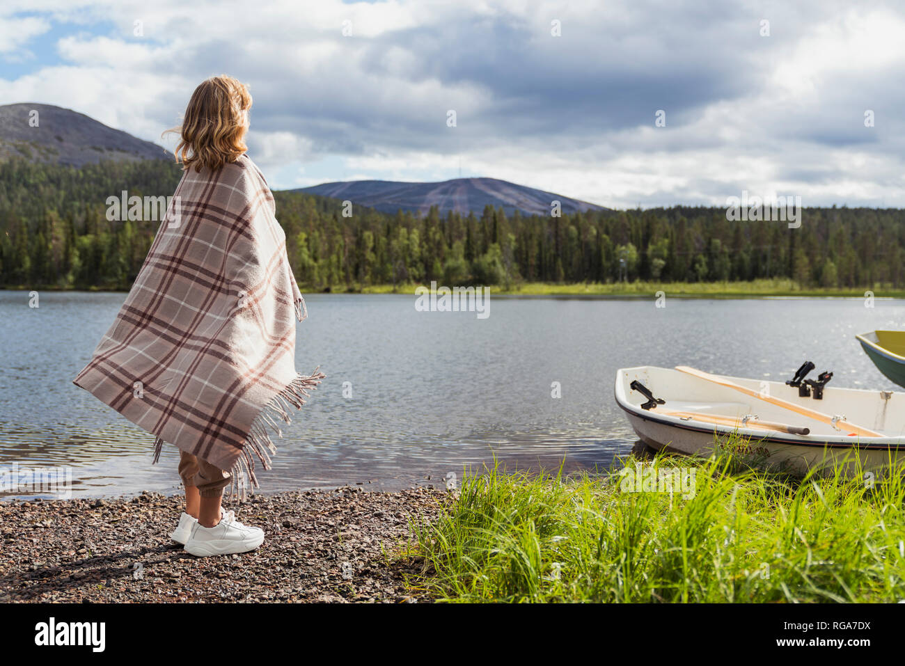 Finland, Lapland, woman wrapped in a blanket standing at the lakeside ...