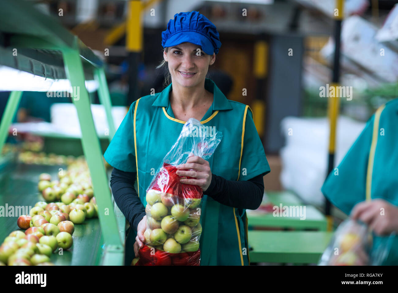 Portrait of smiling woman holding apples in plastic bags in factory ...