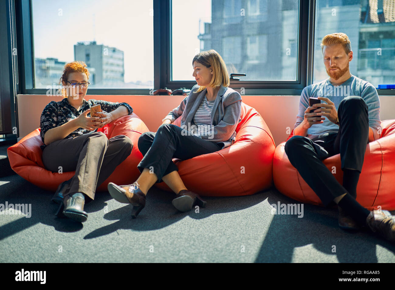 Colleagues with cell phones sitting in bean bags in office lounge Stock ...