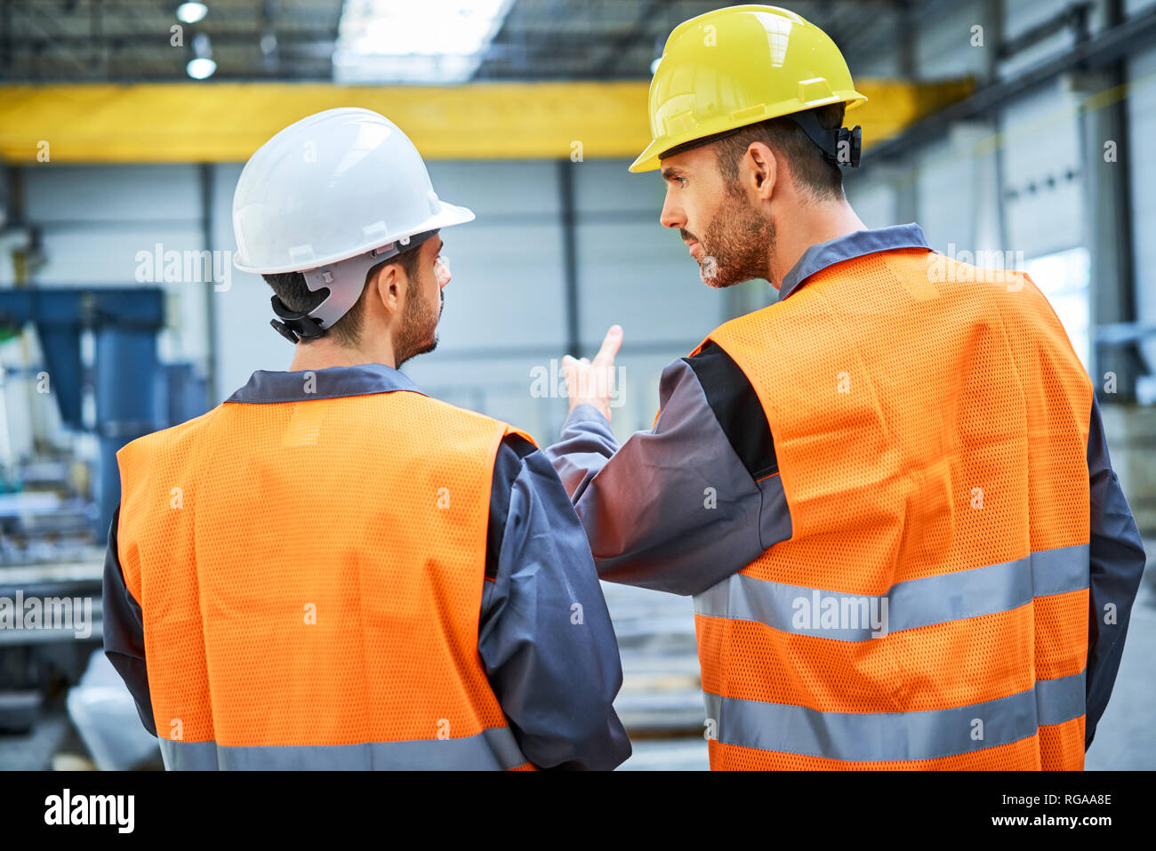 Rear view of two men wearing protective workwear talking in factory ...