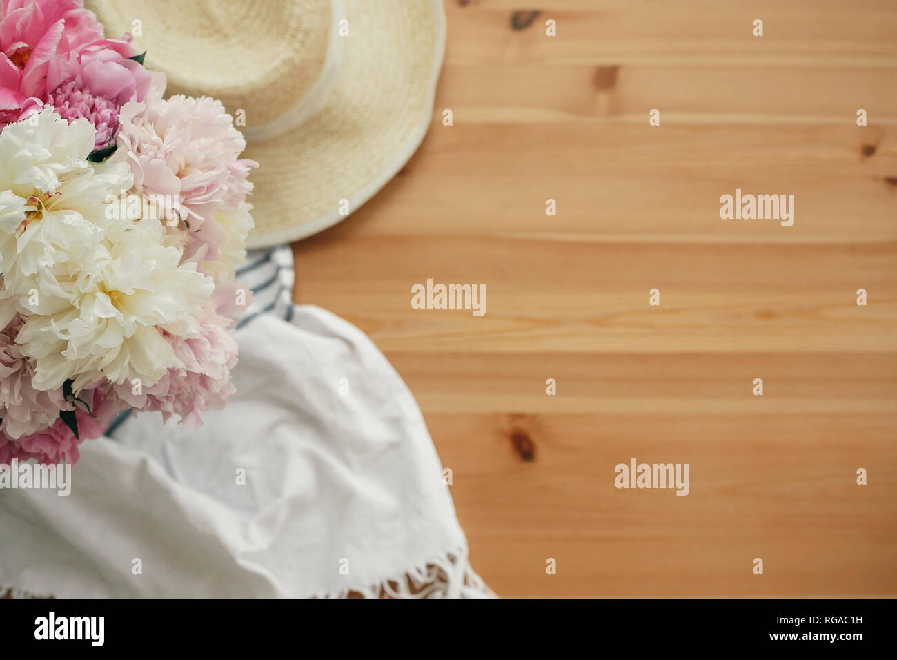 Beautiful peonies in vase and straw hat on rustic wooden table top view ...