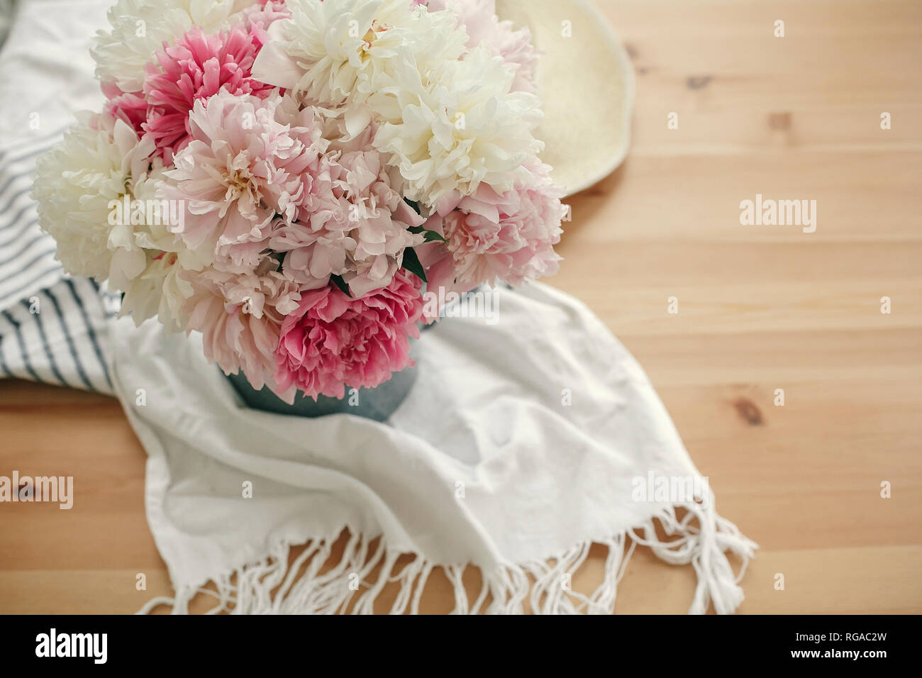 Beautiful peonies in vase and petals on cloth on rustic wooden table ...