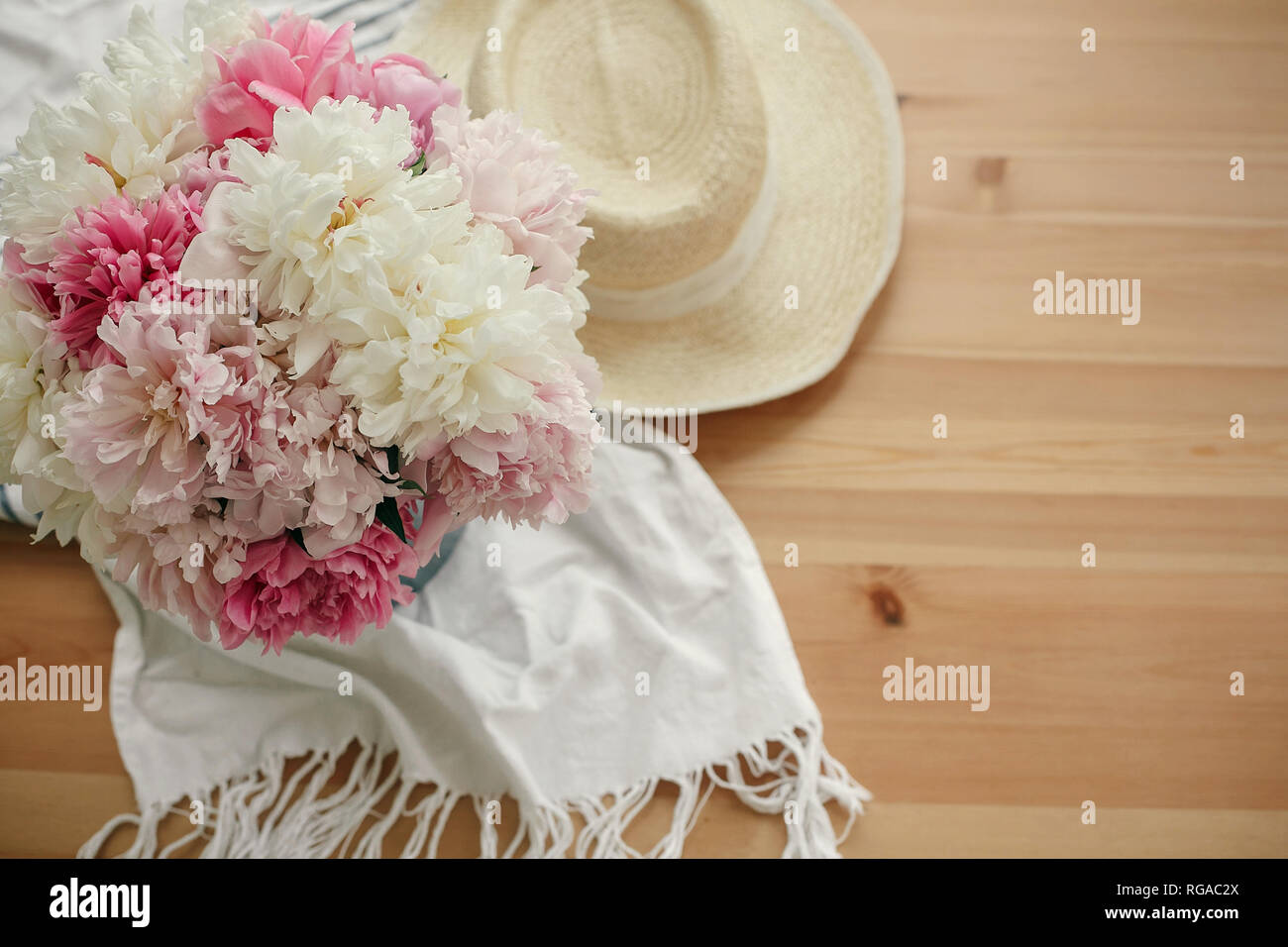 Beautiful peonies in vase and straw hat on rustic wooden table top view ...