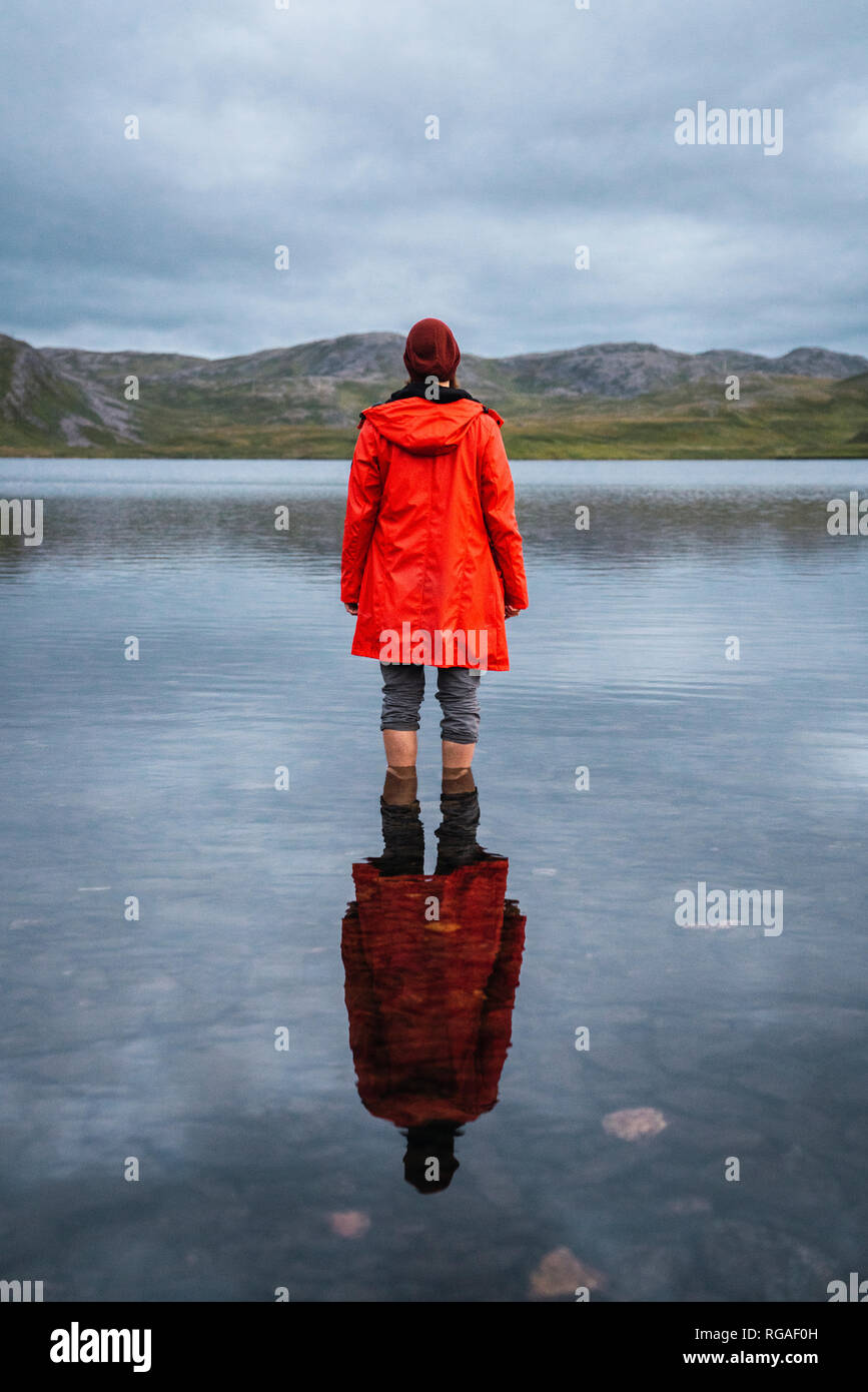 Young man standing ankle deep in water, looking at distance, rear view ...