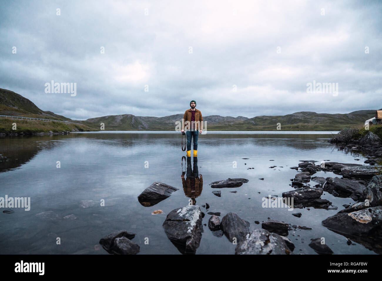 Young man standing ankle deep in water, holding camera Stock Photo - Alamy
