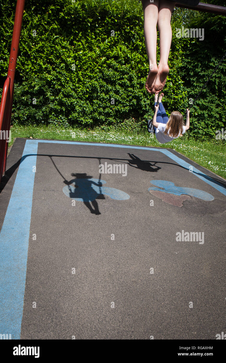 Two caucasion girls playing on swings in a park in a playground with their shadow Stock Photo ...
