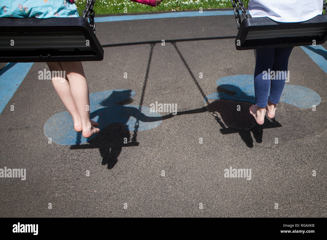 Shadow of two caucasion girls playing on swings in a park in a ...