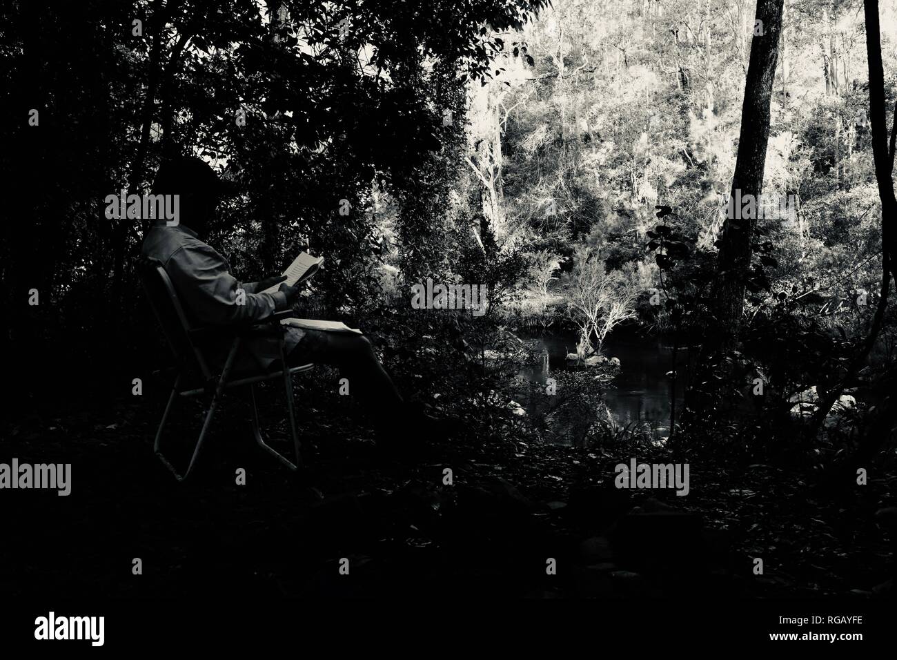 A young man reads a book next to a river, Bush camp at The Diggings ...