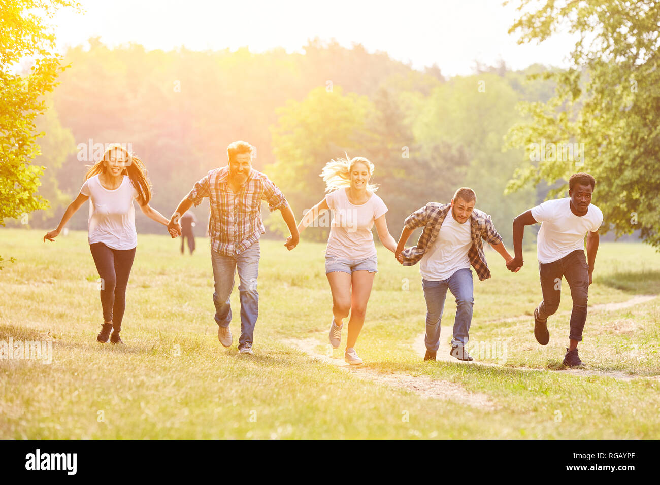 Group of friends holds hands while running as human chain in summer ...