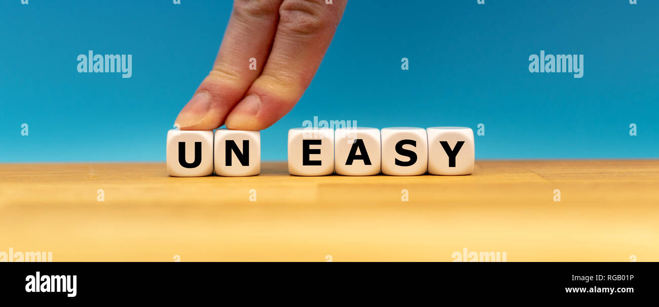 Dice form the word "UNEASY" while two fingers push the letters "UN ...