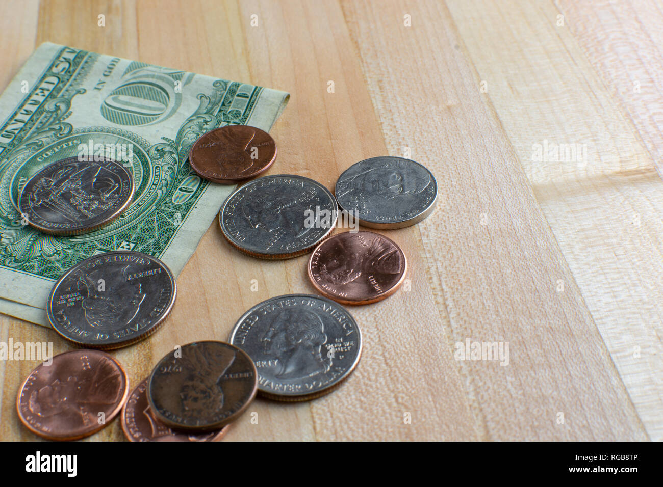 Pocket change and a folded dollar bill placed onto a wooden table. USA ...