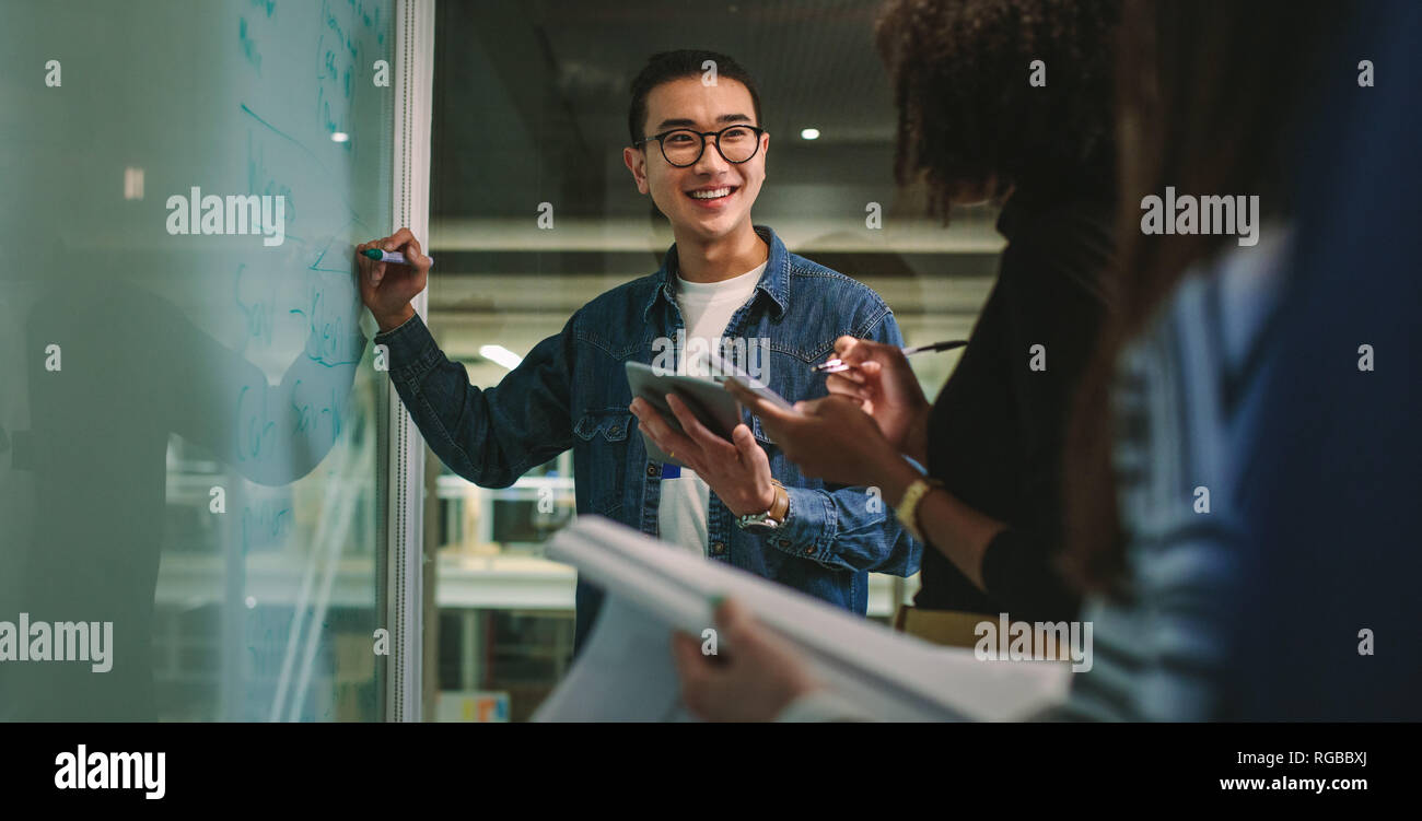 Student writing on glass board in classroom. Male student writing on ...