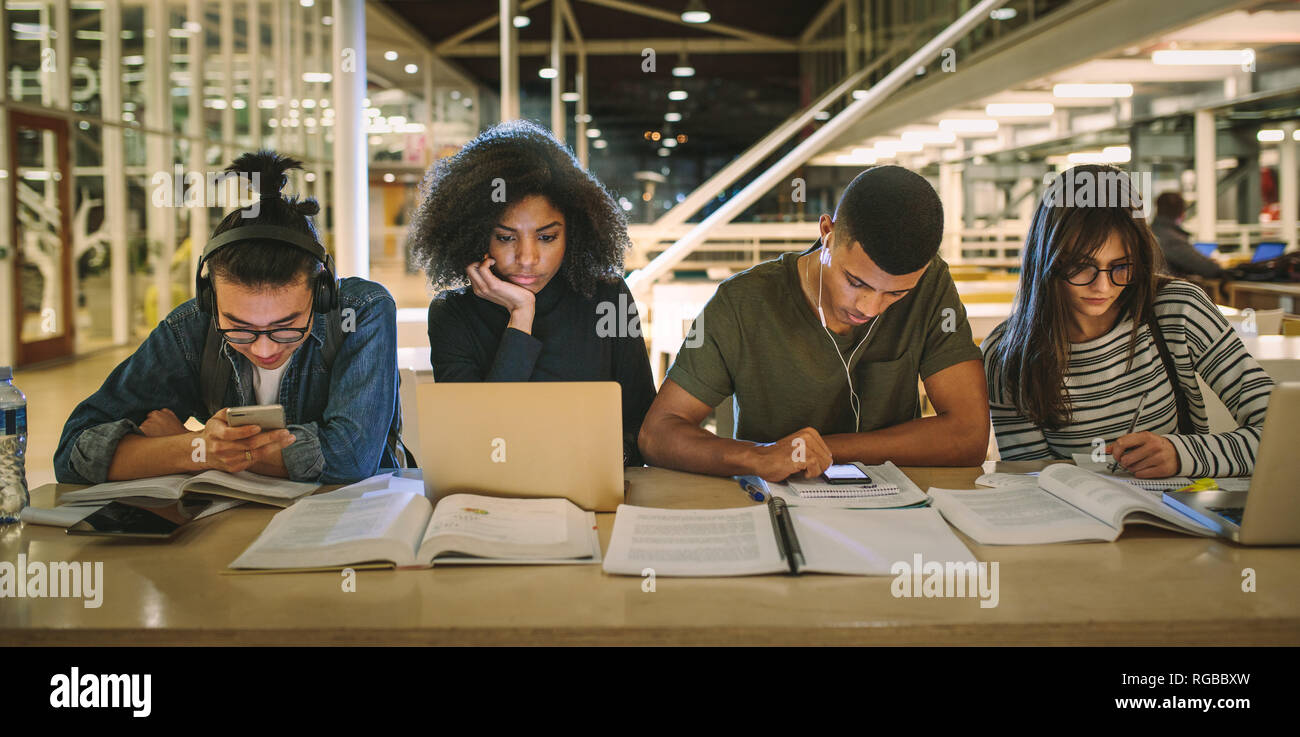 Multi-ethnic students sitting at college library. Students using making ...