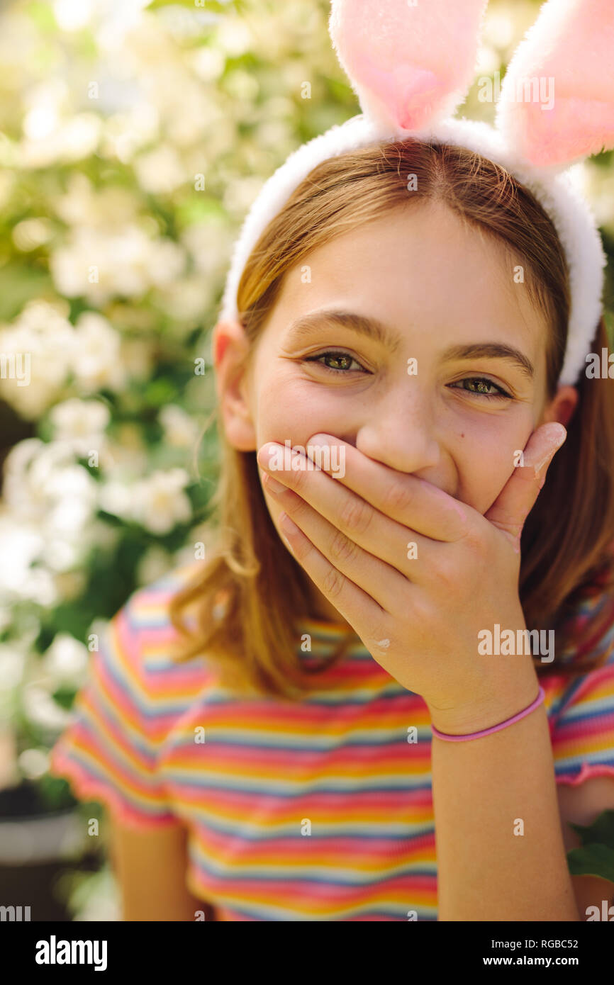 Portrait of a girl wearing rabbit ear headband laughing covering her ...