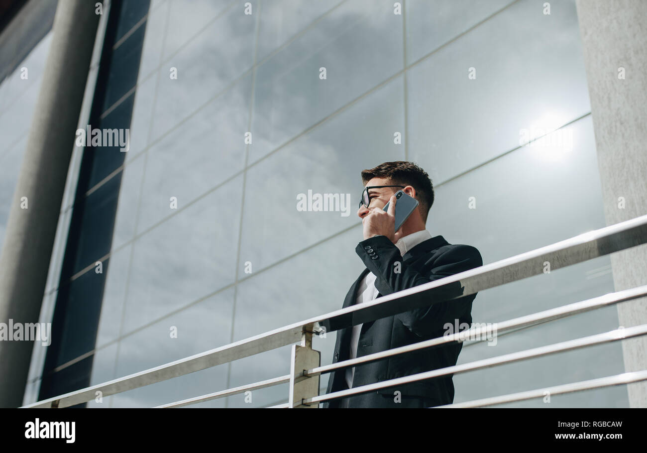 businessman talking over cell phone standing in front of a glass facade ...